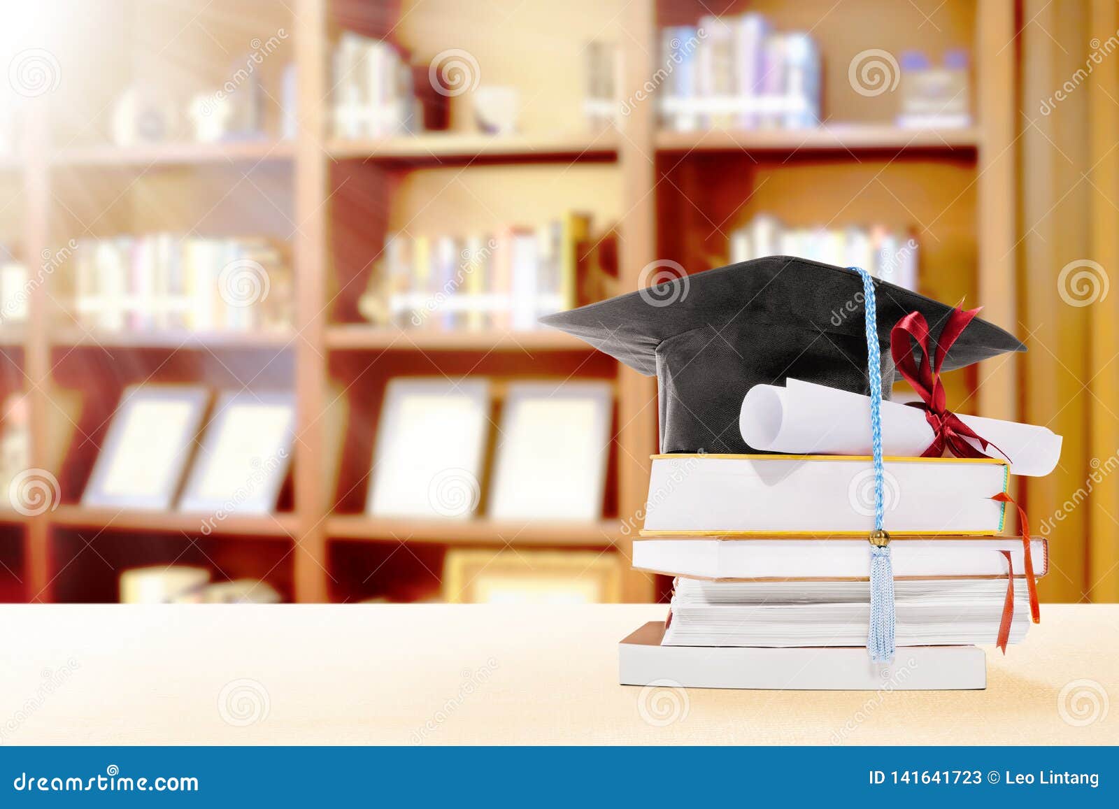 Graduation Hat, Diploma Scroll and Books on the Table with Bookshelf ...