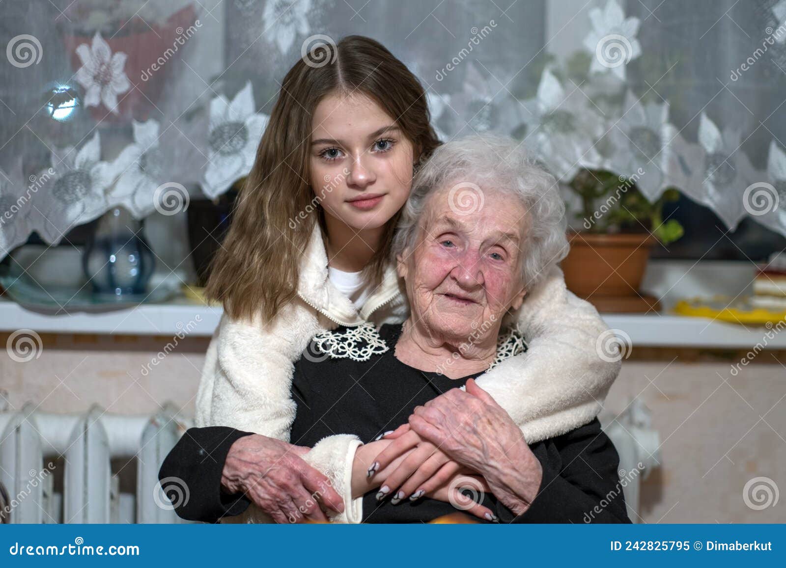 Granddaughter Hugs Old Grandmother Sitting On A Chair Stock Image