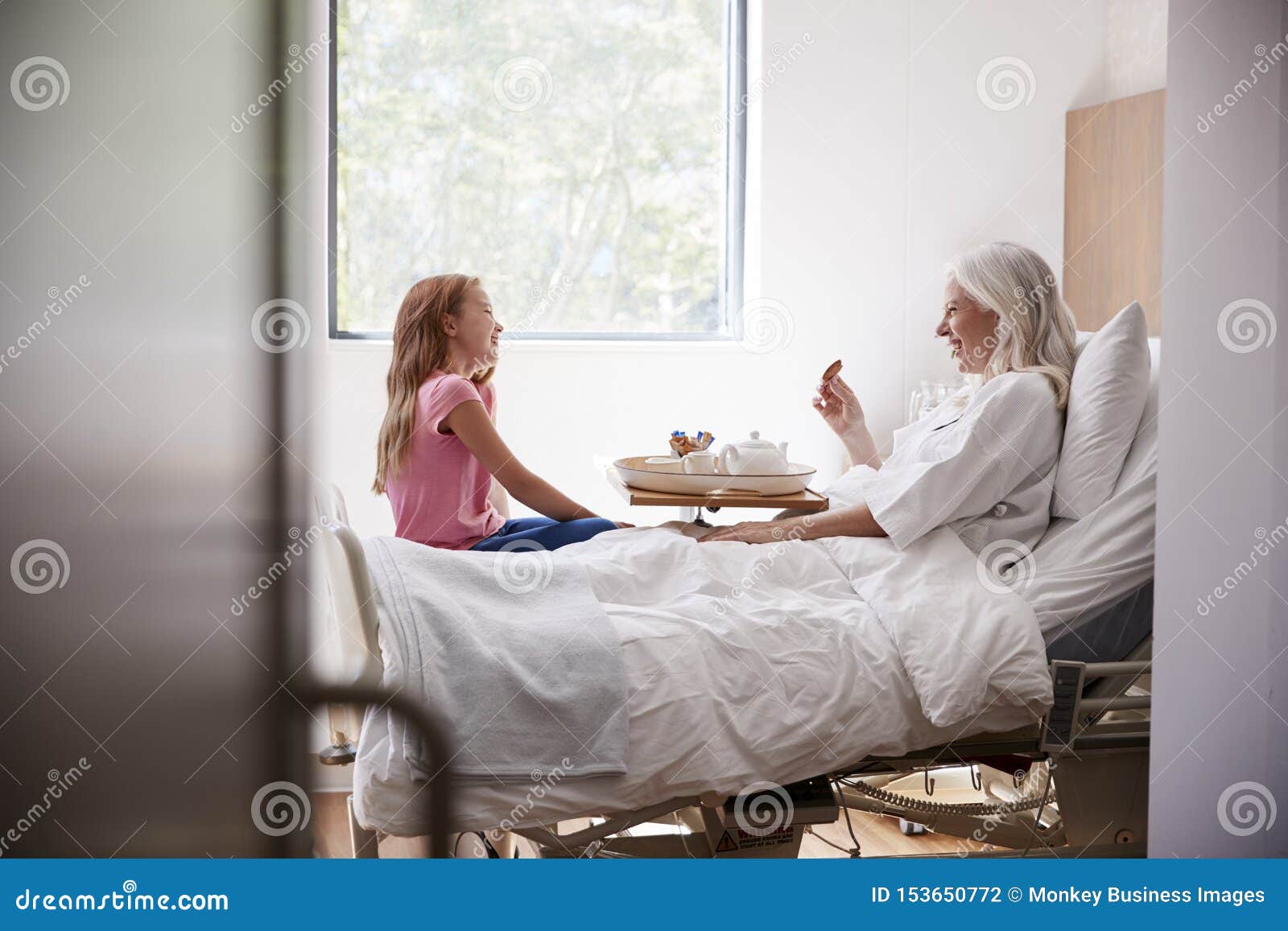 Granddaughter Visiting Grandmother In Hospital Bed For Afternoon Tea