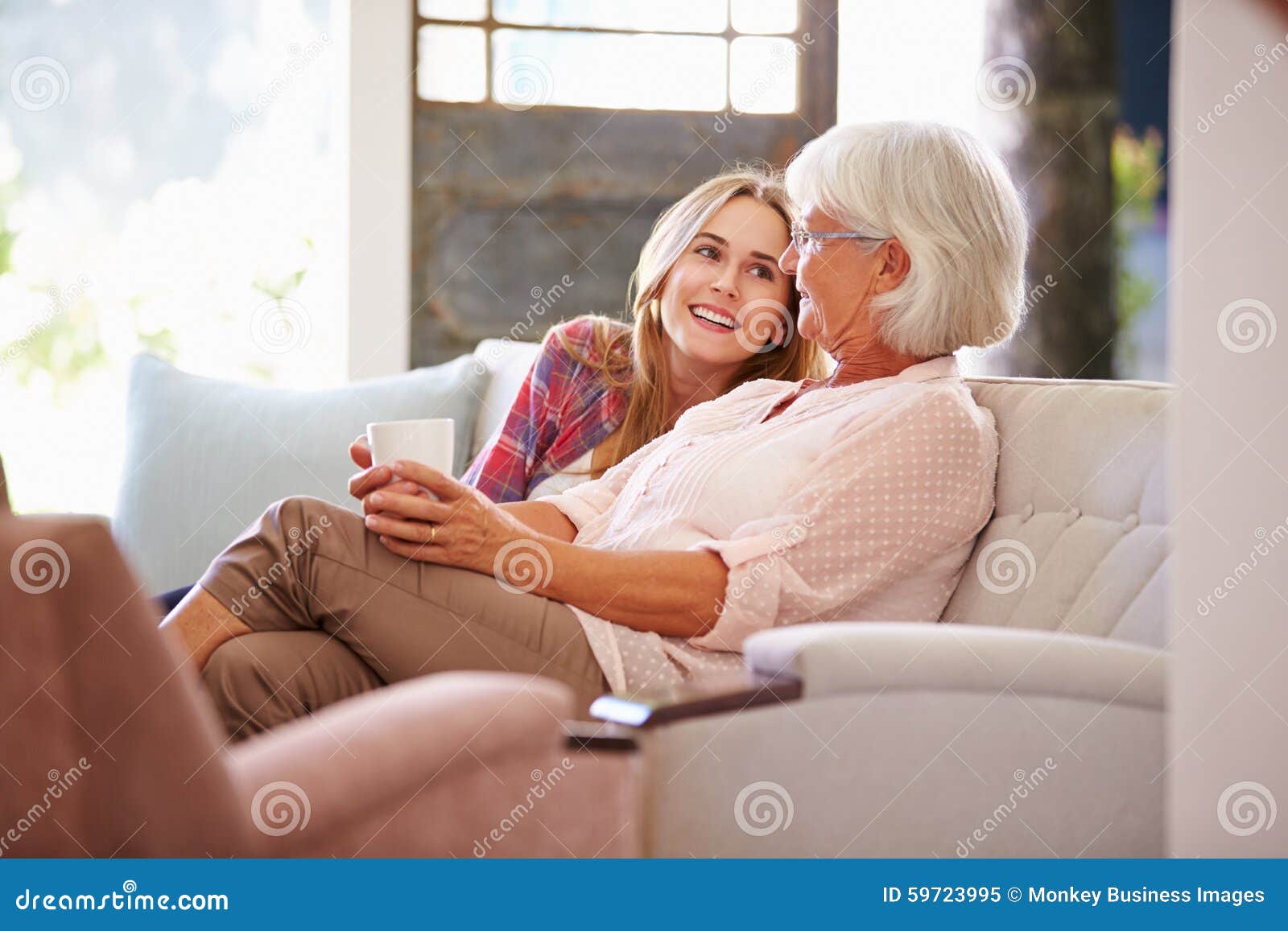 Grandmother With Adult Granddaughter Relaxing On Sofa Stock Image