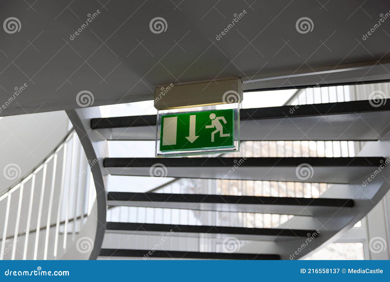Green Emergency Exit Sign Under a Spiral Staircase with Railing, by Day ...