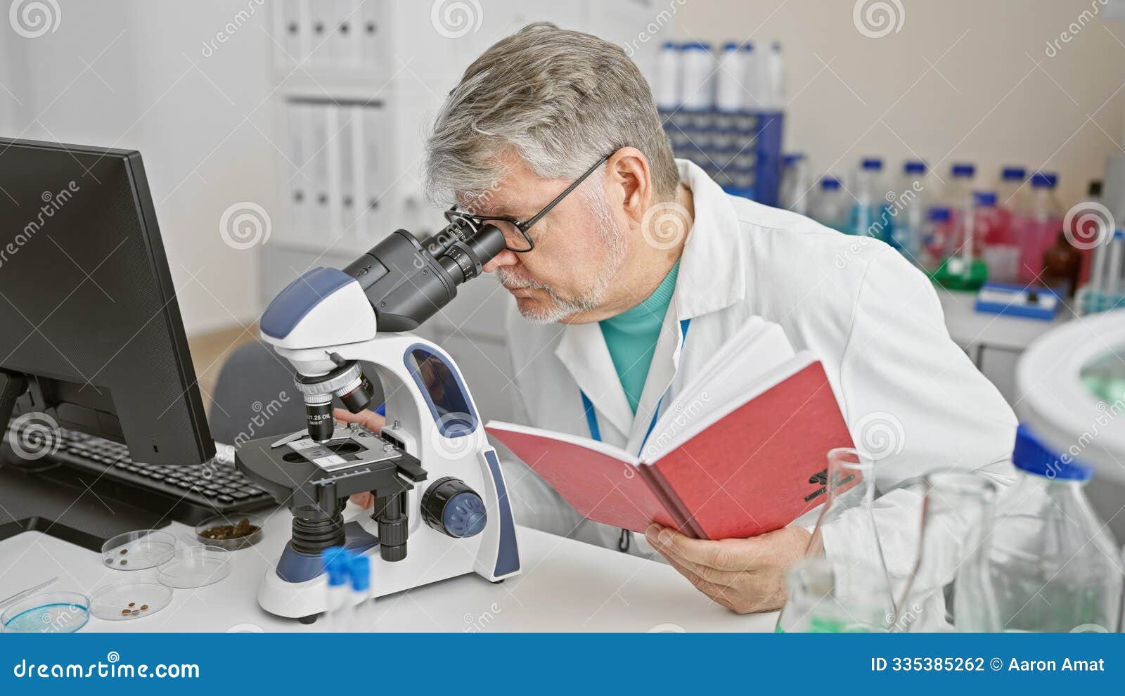 Grey-haired Man in Lab Coat Using Microscope and Holding a Notebook in ...