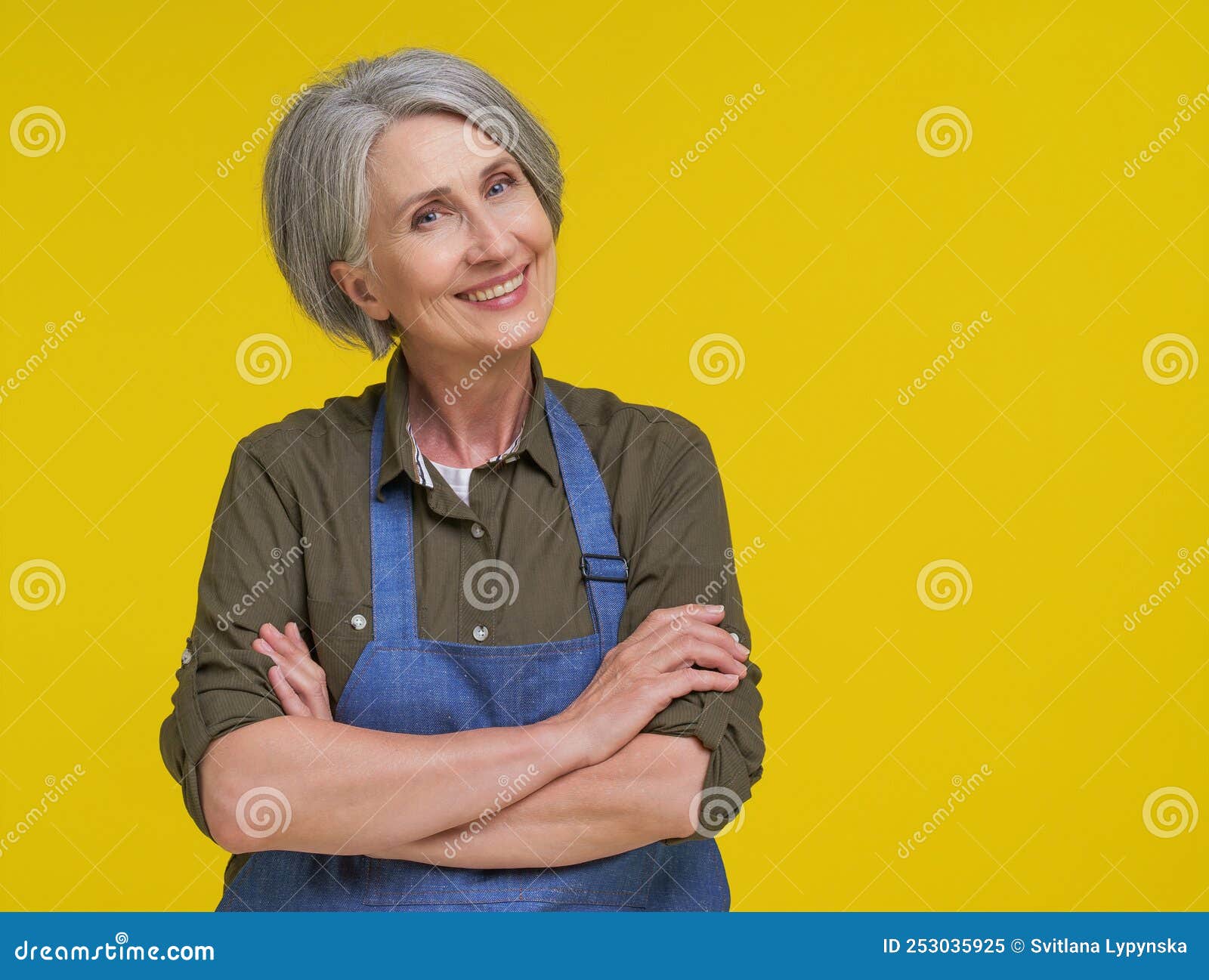 Grey Haired Mature Woman In Denim Apron Standing With Arms Folded