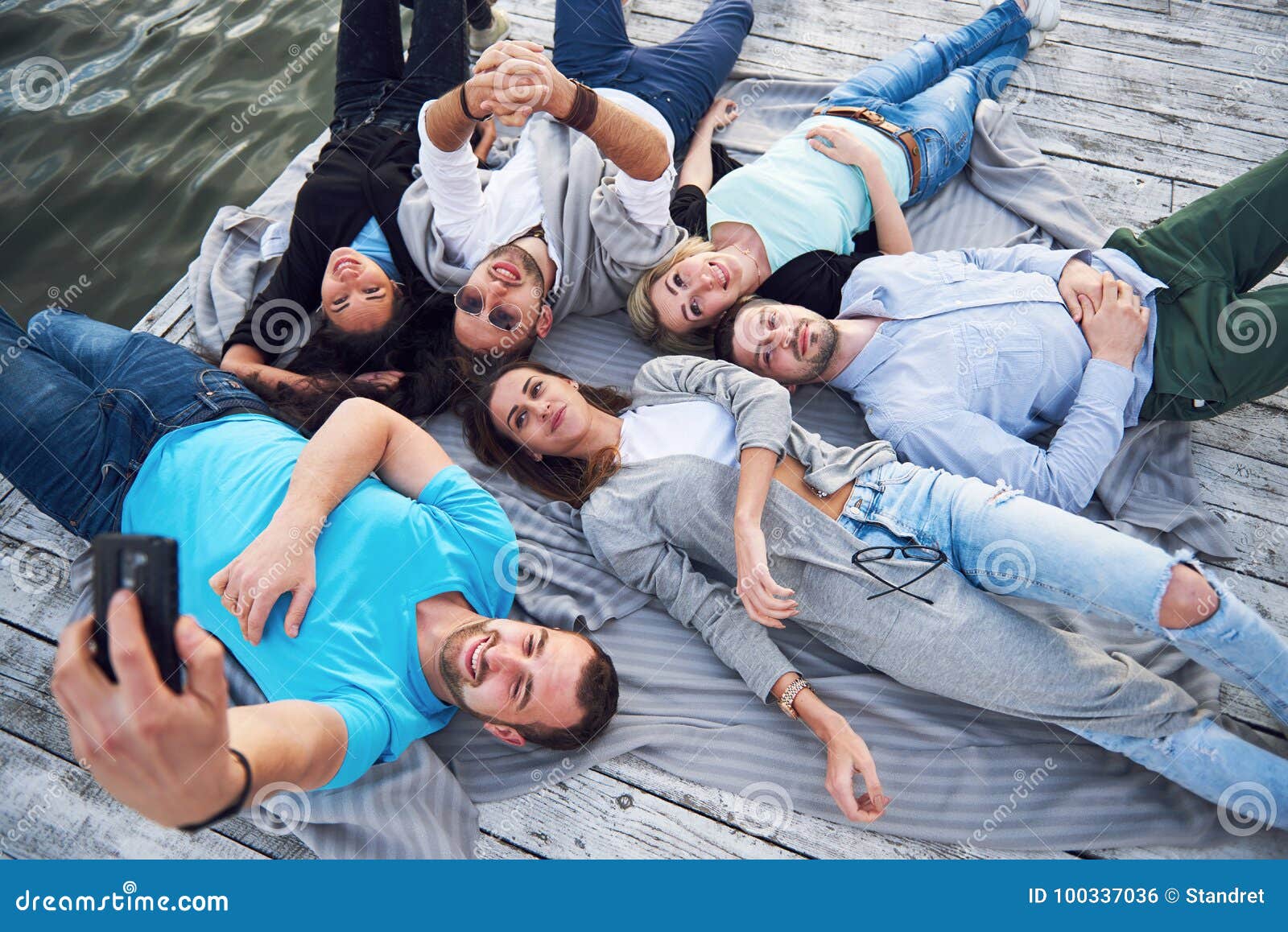 Group Of Beautiful Young People Who Do Selfies Lying On The Pier The