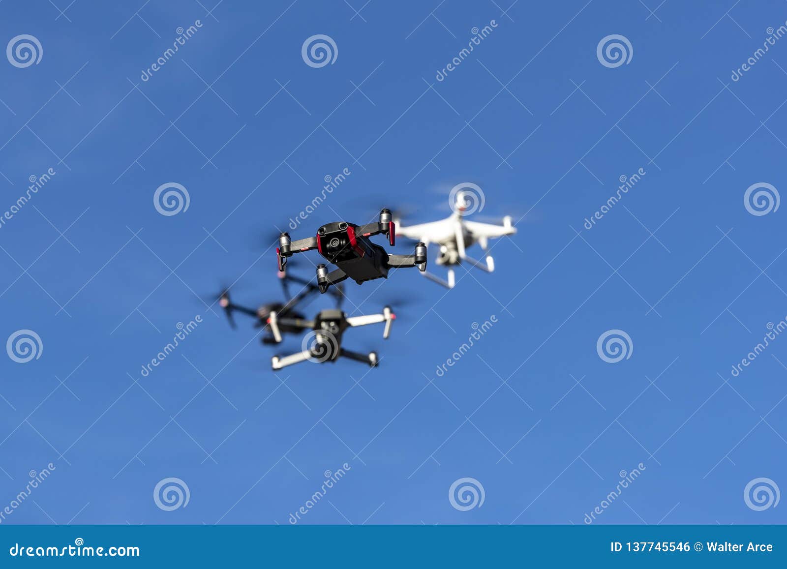 A Group of Multiple Drones Fly Together through the Air Against a Blue ...
