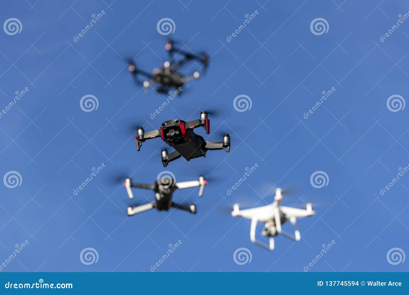 A Group of Multiple Drones Fly Together through the Air Against a Blue ...