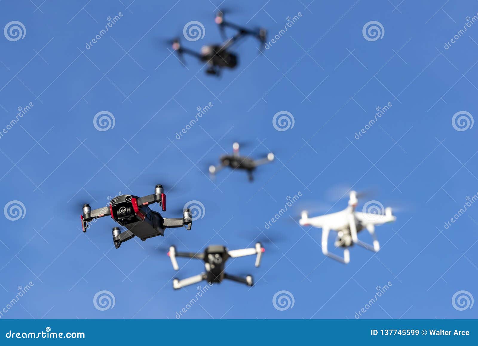 A Group of Multiple Drones Fly Together through the Air Against a Blue ...