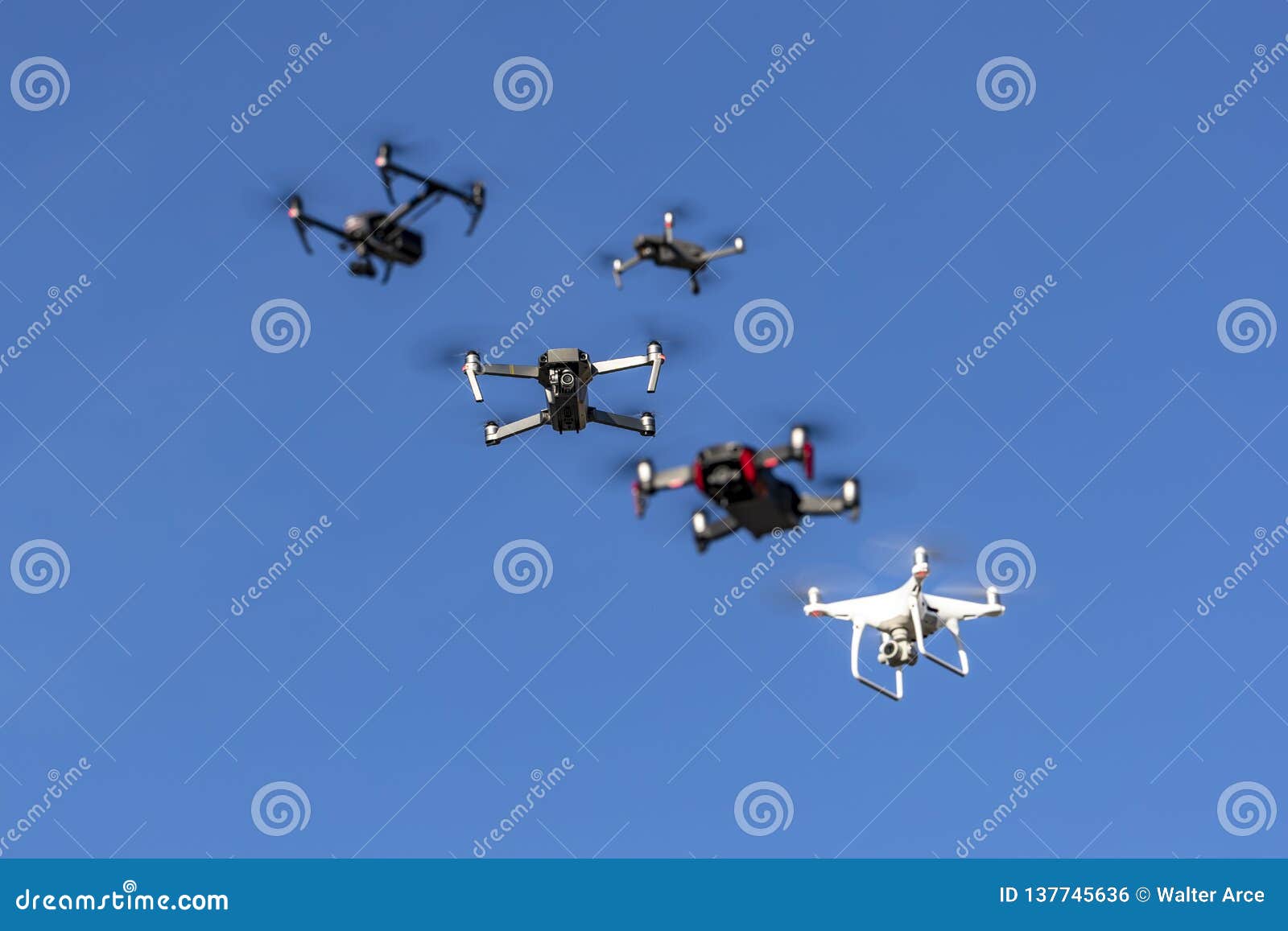 A Group of Multiple Drones Fly Together through the Air Against a Blue ...
