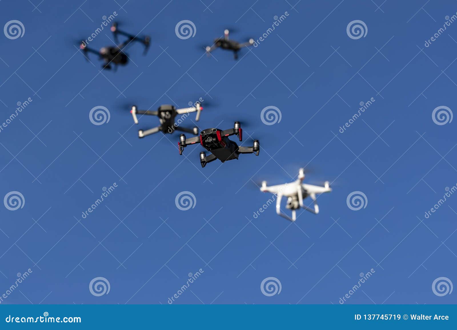 A Group of Multiple Drones Fly Together through the Air Against a Blue ...