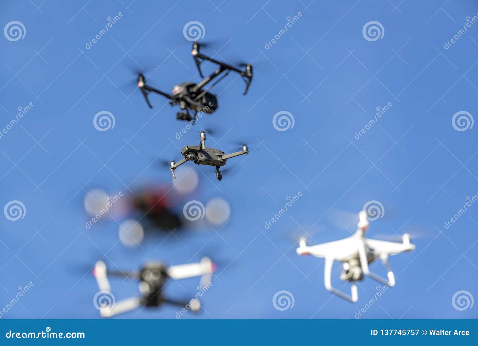 A Group of Multiple Drones Fly Together through the Air Against a Blue ...