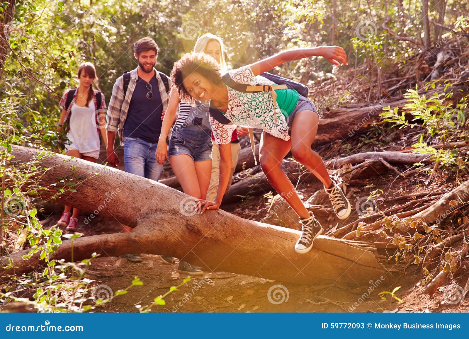 Group of Friends Jumping Over Tree Trunk on Countryside Walk Stock ...