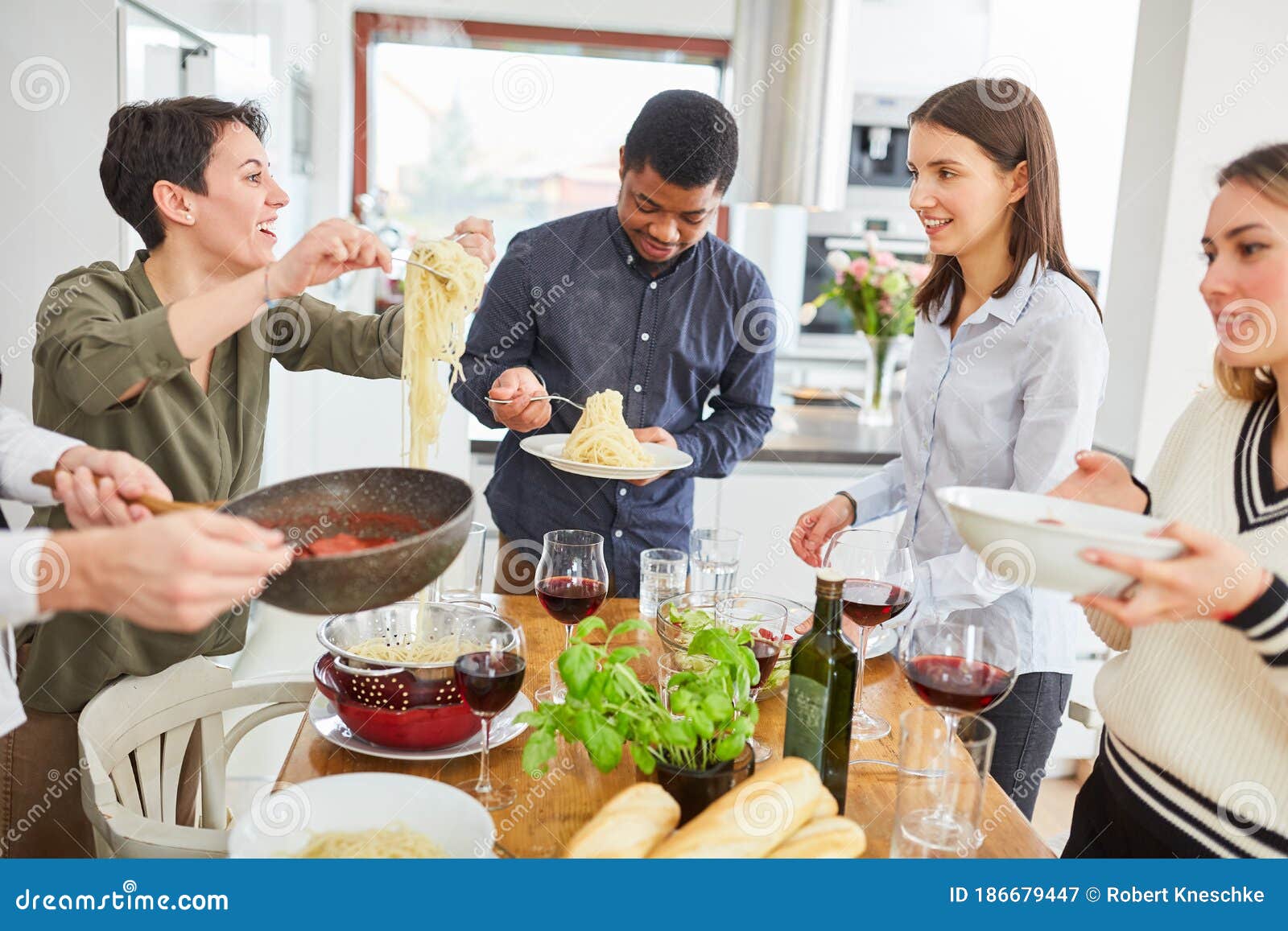 Group of Friends Serving Spaghetti with Tomato Sauce in Kitchen Stock ...