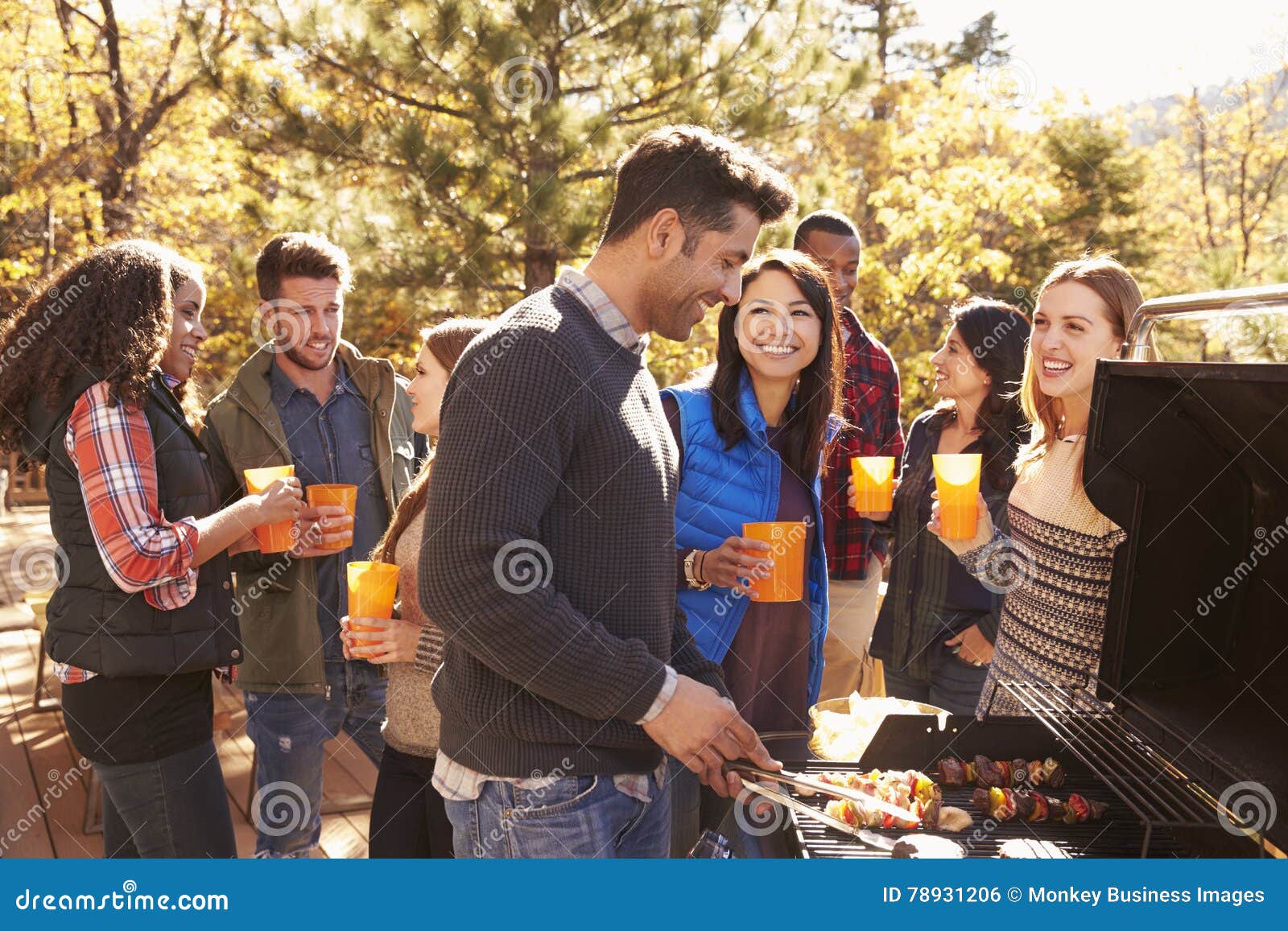 Group of Friends Stand at a Barbecue, One Cooking at Grill Stock Photo ...