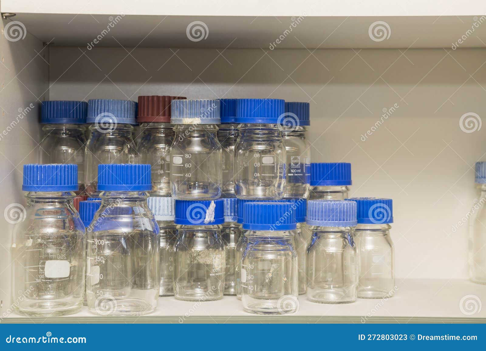 A Group of Glass Laboratory Bottles with Bleu Caps on a Shelve. Stock ...
