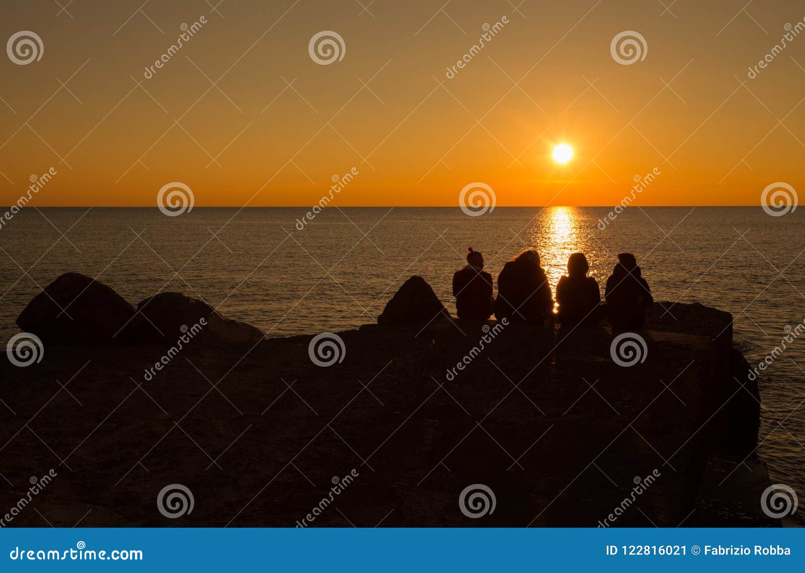 A Group of People Sit Down Looking at Sunset in Front of the Sea ...