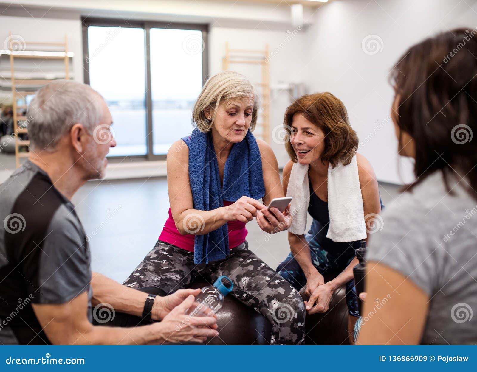A Group of Seniors with Smartphone in Gym Resting after Doing Exercise ...