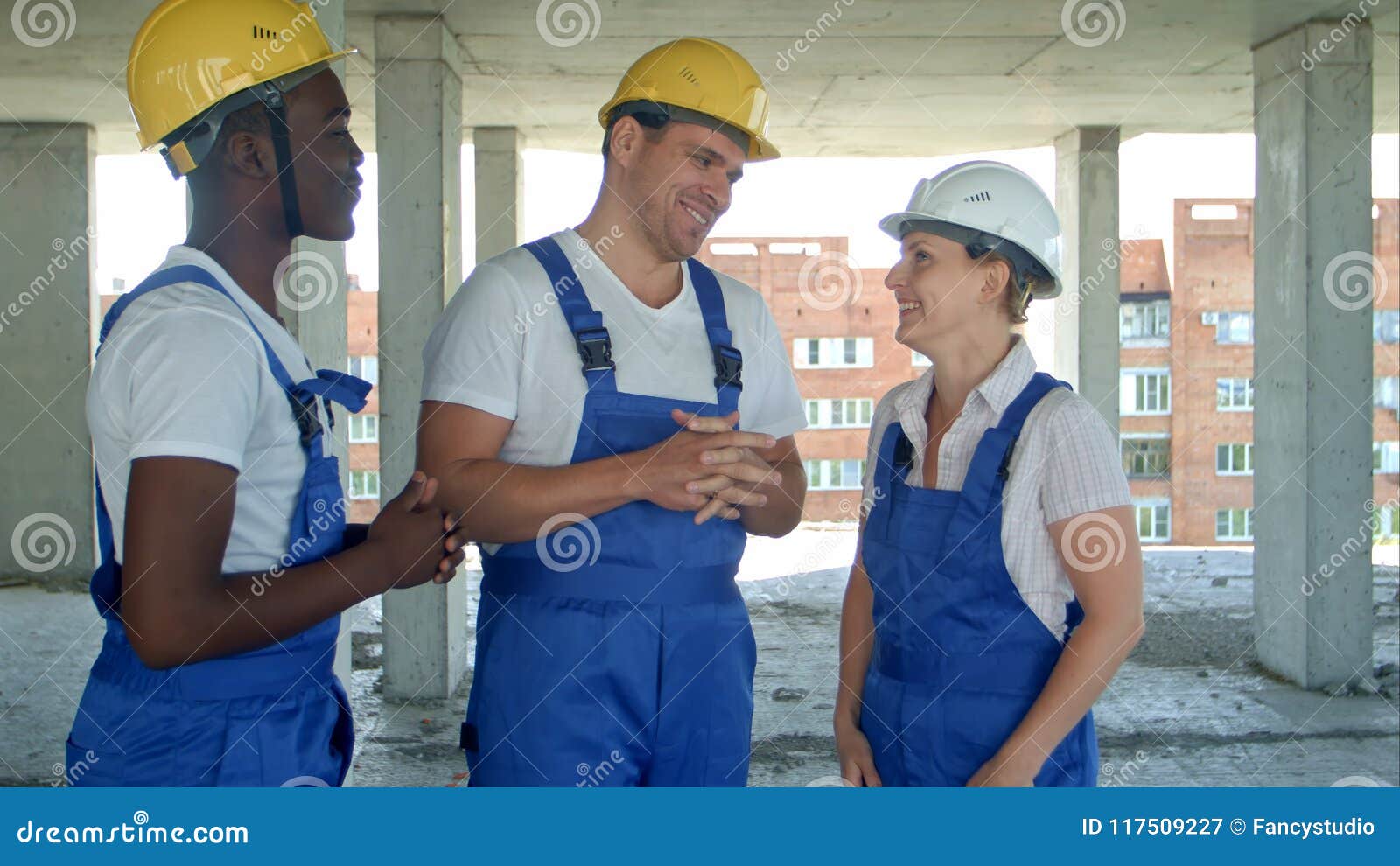 Group of Smiling Builders in Hardhats Talking at Construction Site ...
