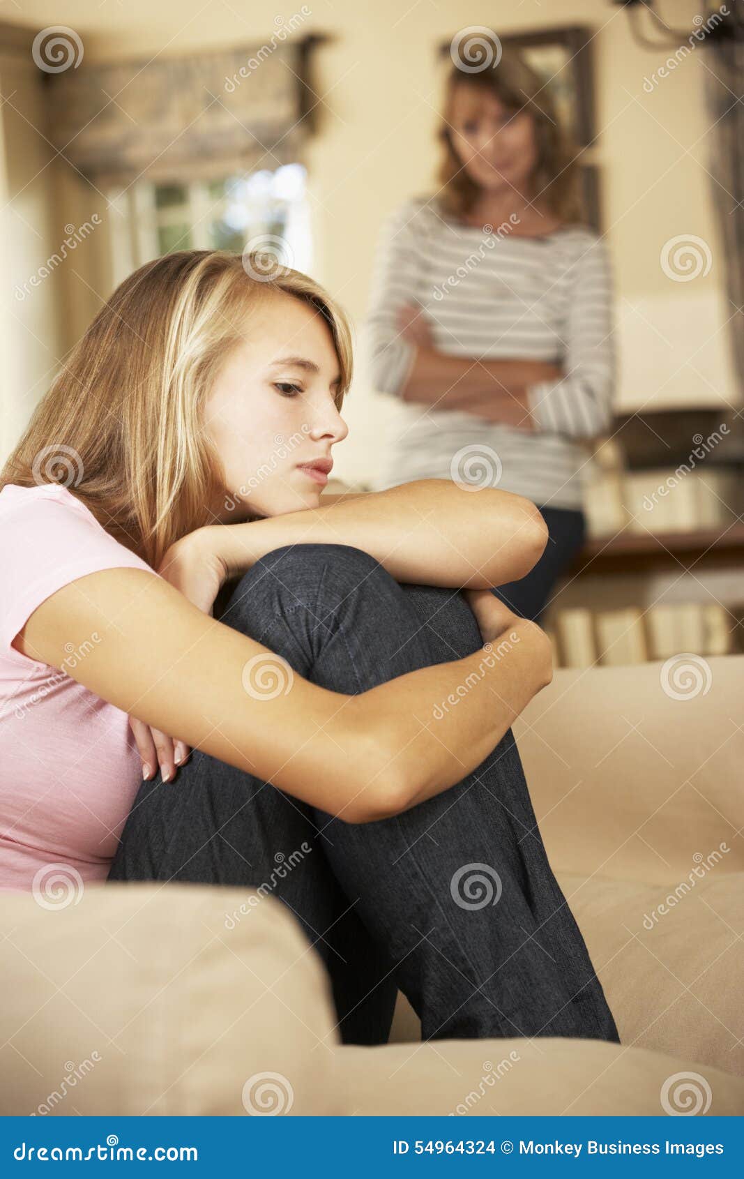 Grumpy Teenage Daughter Sitting on Sofa with Mother in Background Stock ...