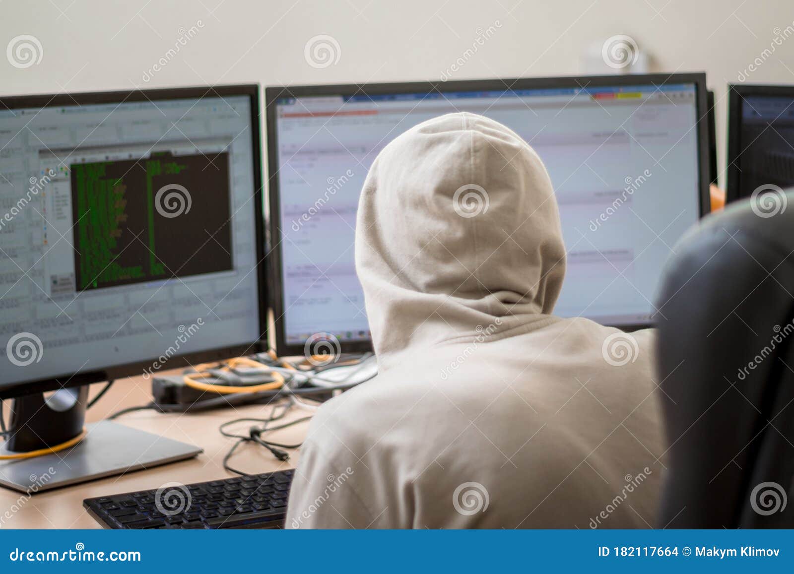 A Hacker in a Hood Sits in Front of Several Monitors. the View from the ...