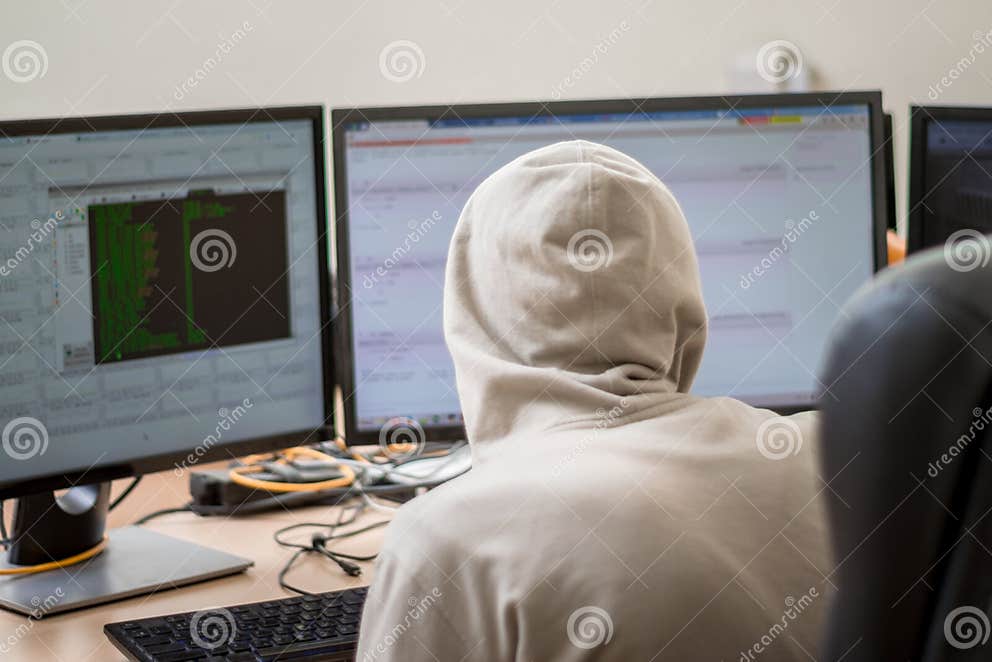 A Hacker in a Hood Sits in Front of Several Monitors. the View from the ...