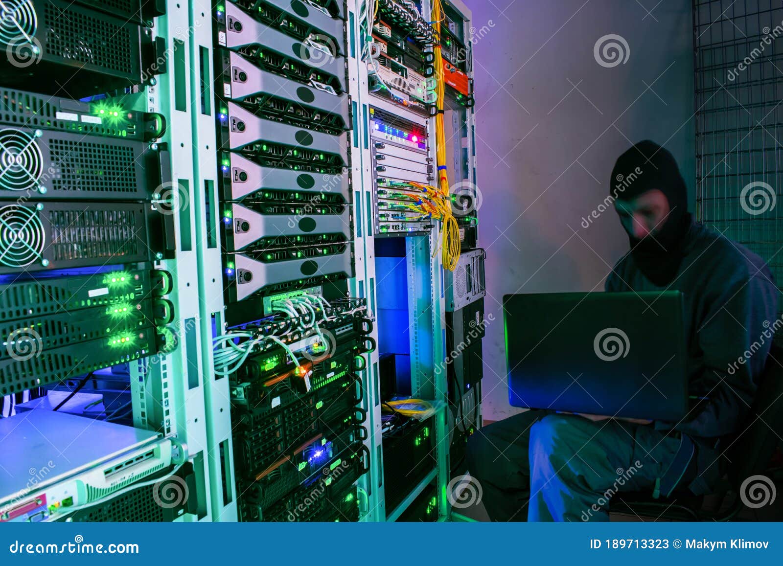 The Hacker in a Mask with Laptop Performs the Attack, Sitting on a ...