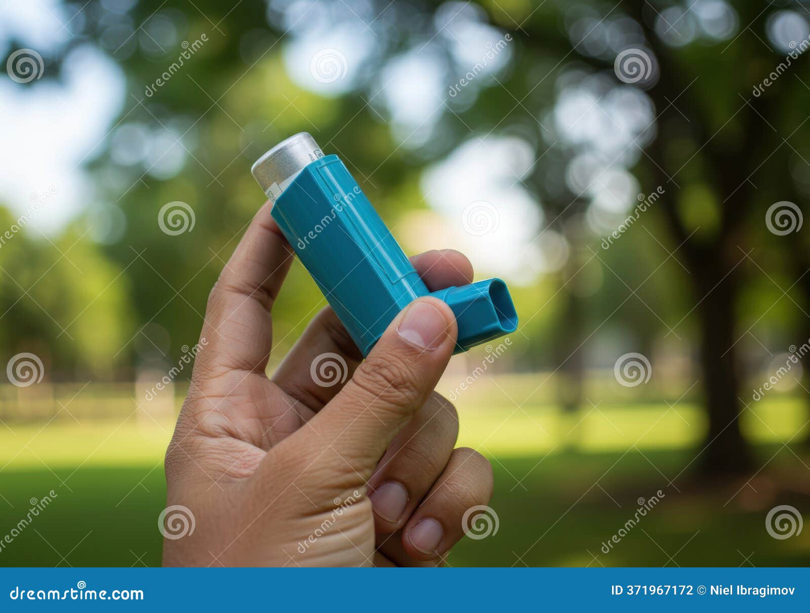 Hand Holding Blue Asthma Inhaler In Park Setting With Green Trees In ...
