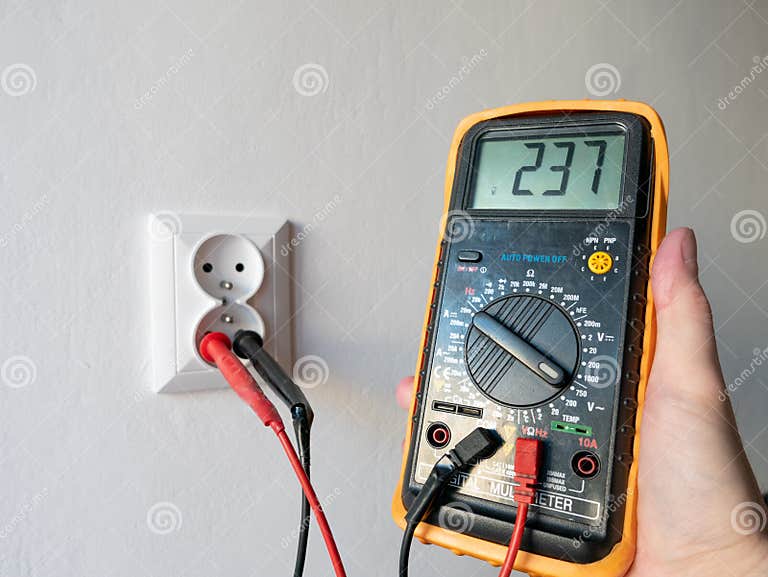 Hand Holding an Electric Multimeter in Front of the Electric Socket ...