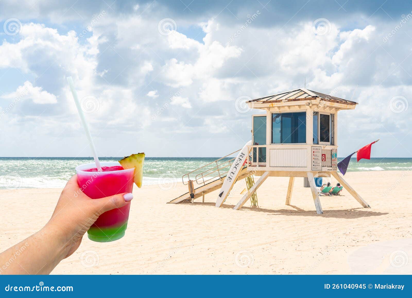 Hand Holding Glass With Cocktail And Straw With Lifeguard Cabin At