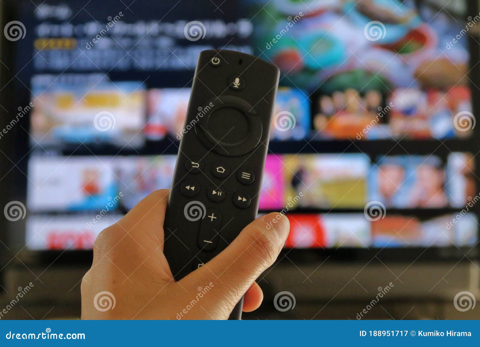 A Hand is Holding a Remote Controller with a TV Screen in Background ...