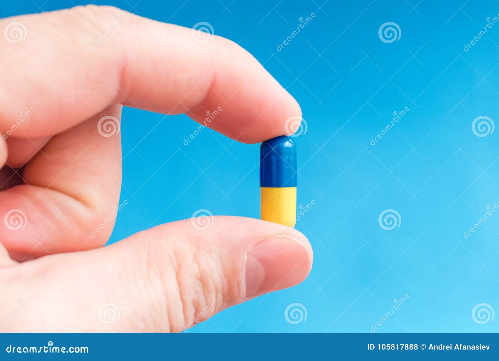 A Hand Holds a Blue-yellow Capsule Pill on a Blue Background Stock ...