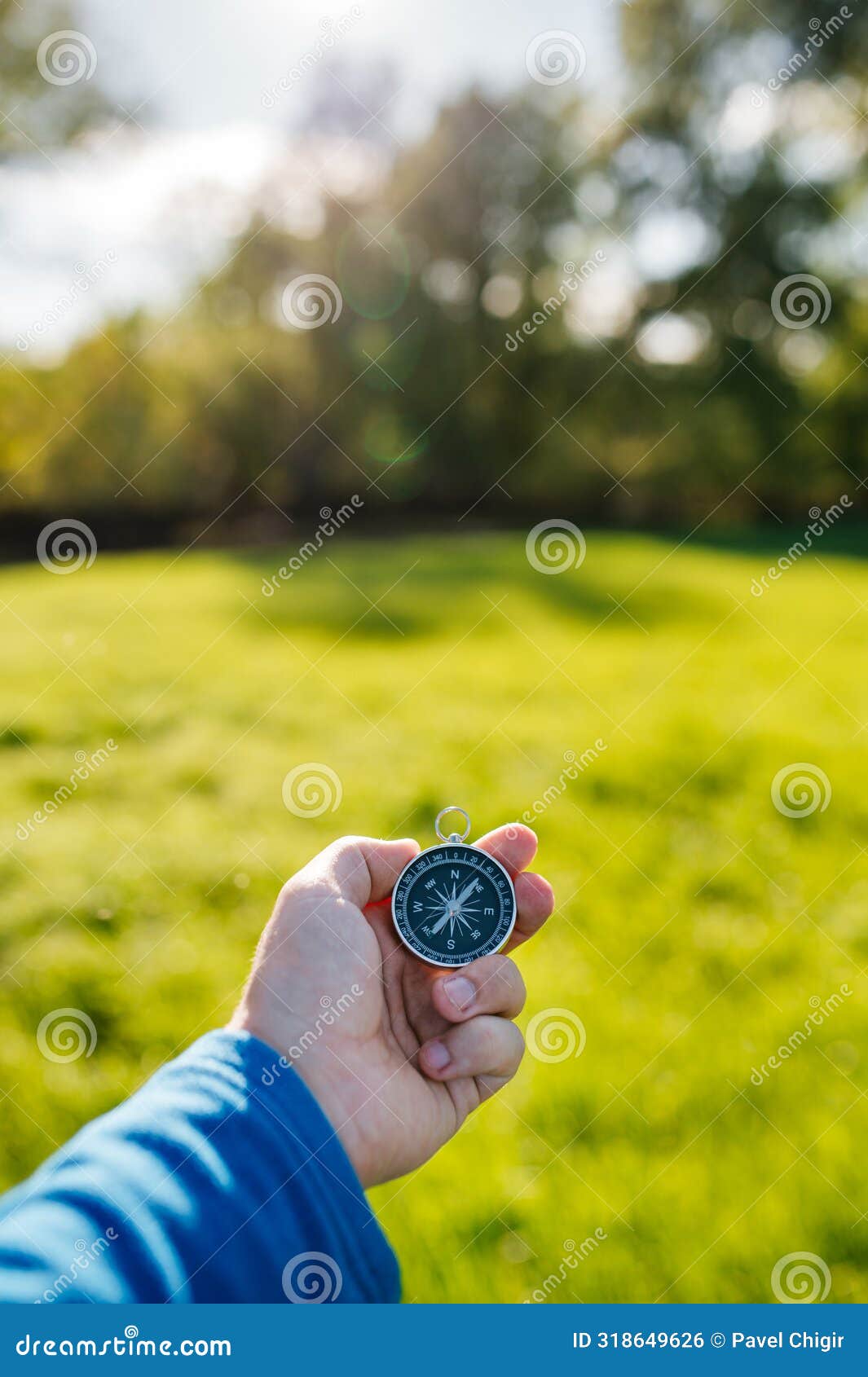 A Hand Holds a Compass Against a Background of Green Grass and Trees ...