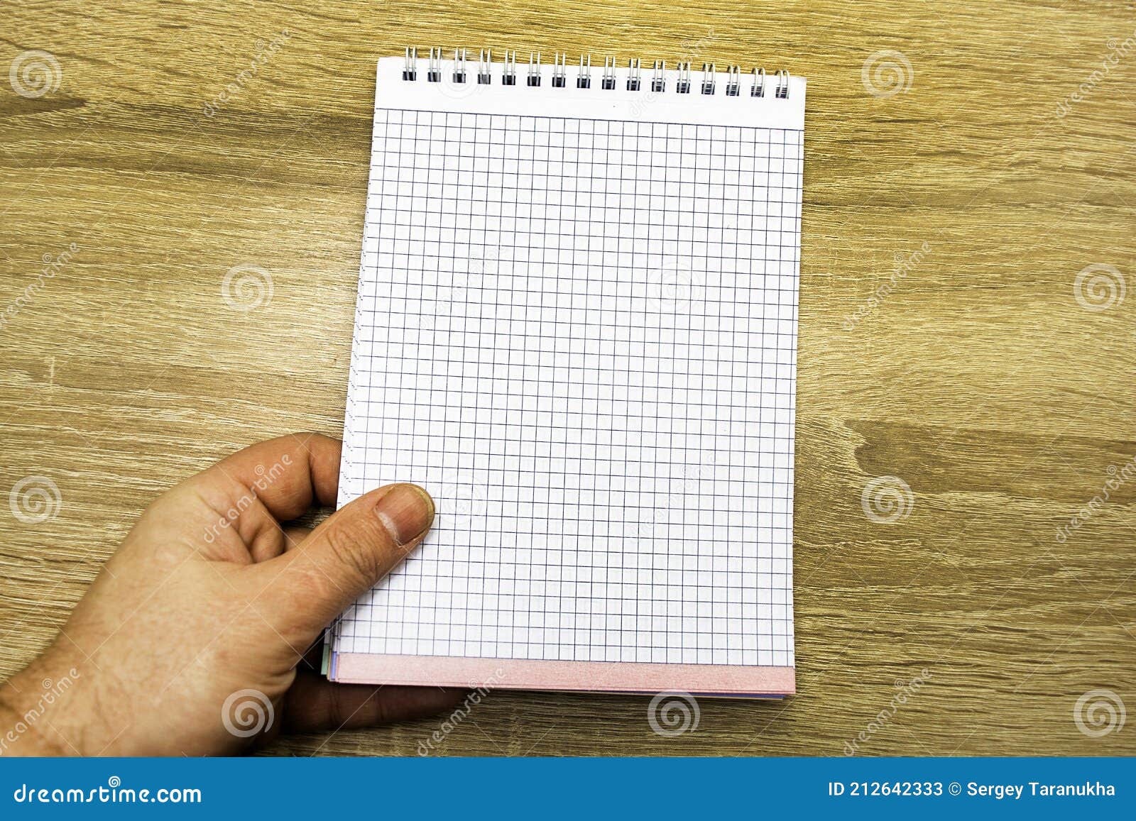 A Hand Holds an Open Notebook for Writing on the Background of a Wooden ...