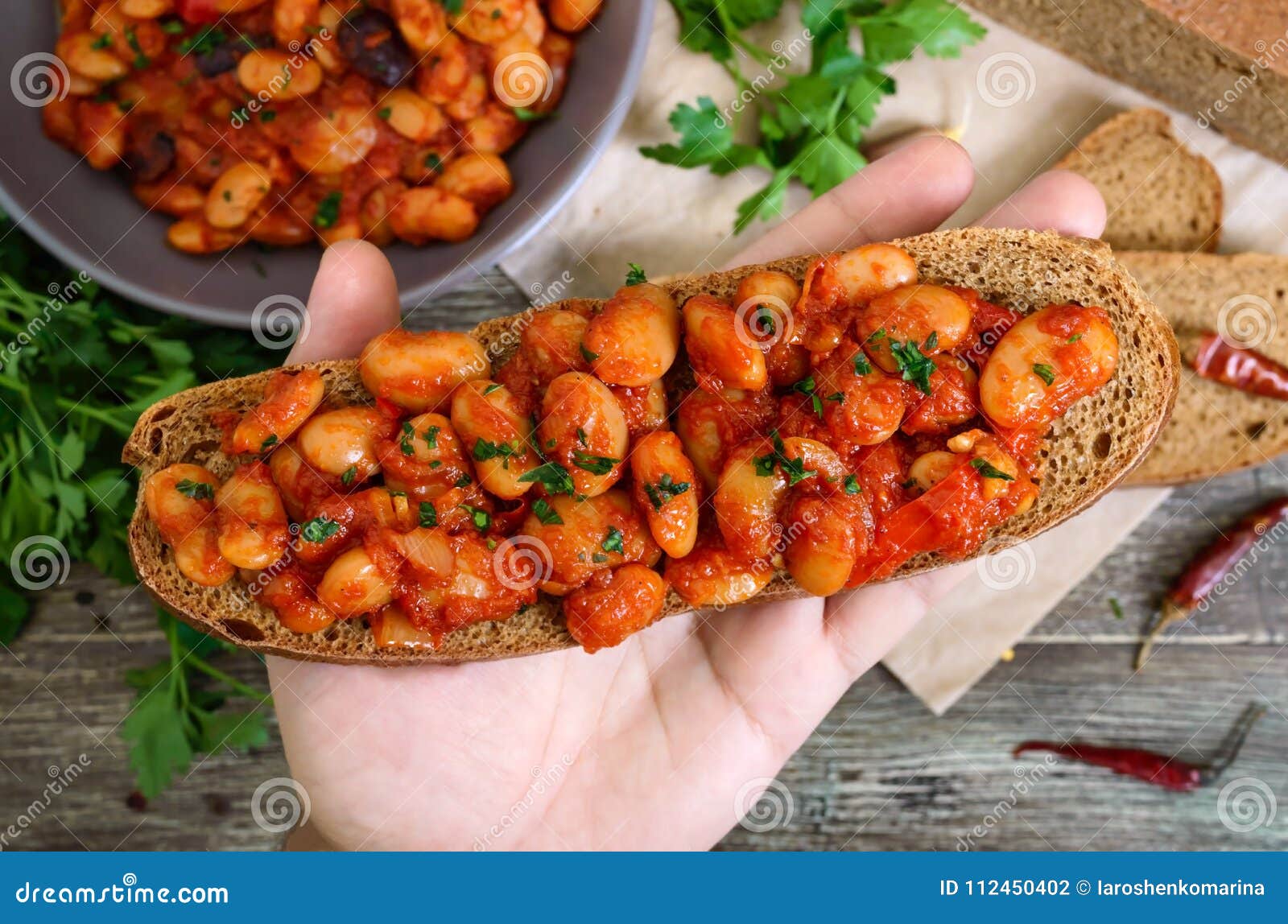 The Hand Holds a Piece of Rye Bread with Beans in the Background of the ...