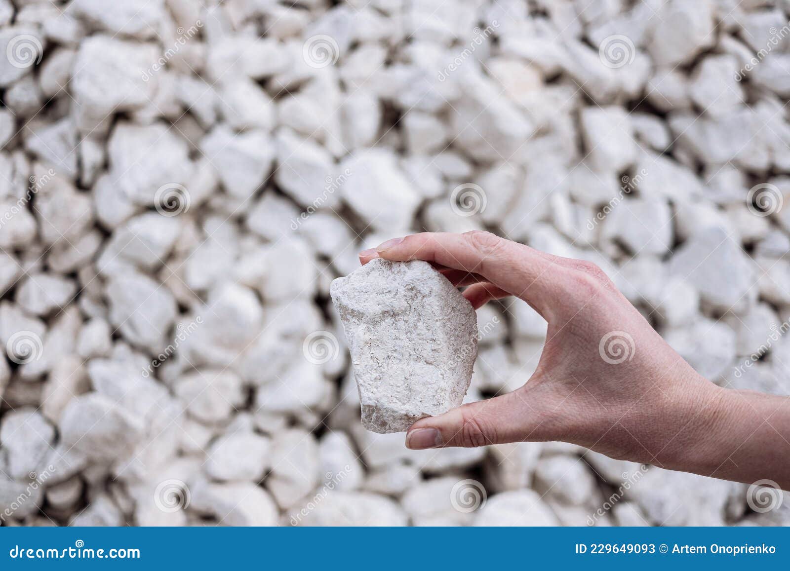 Hand Holds a White Chalkstone with a Lot of Stones on the Background ...