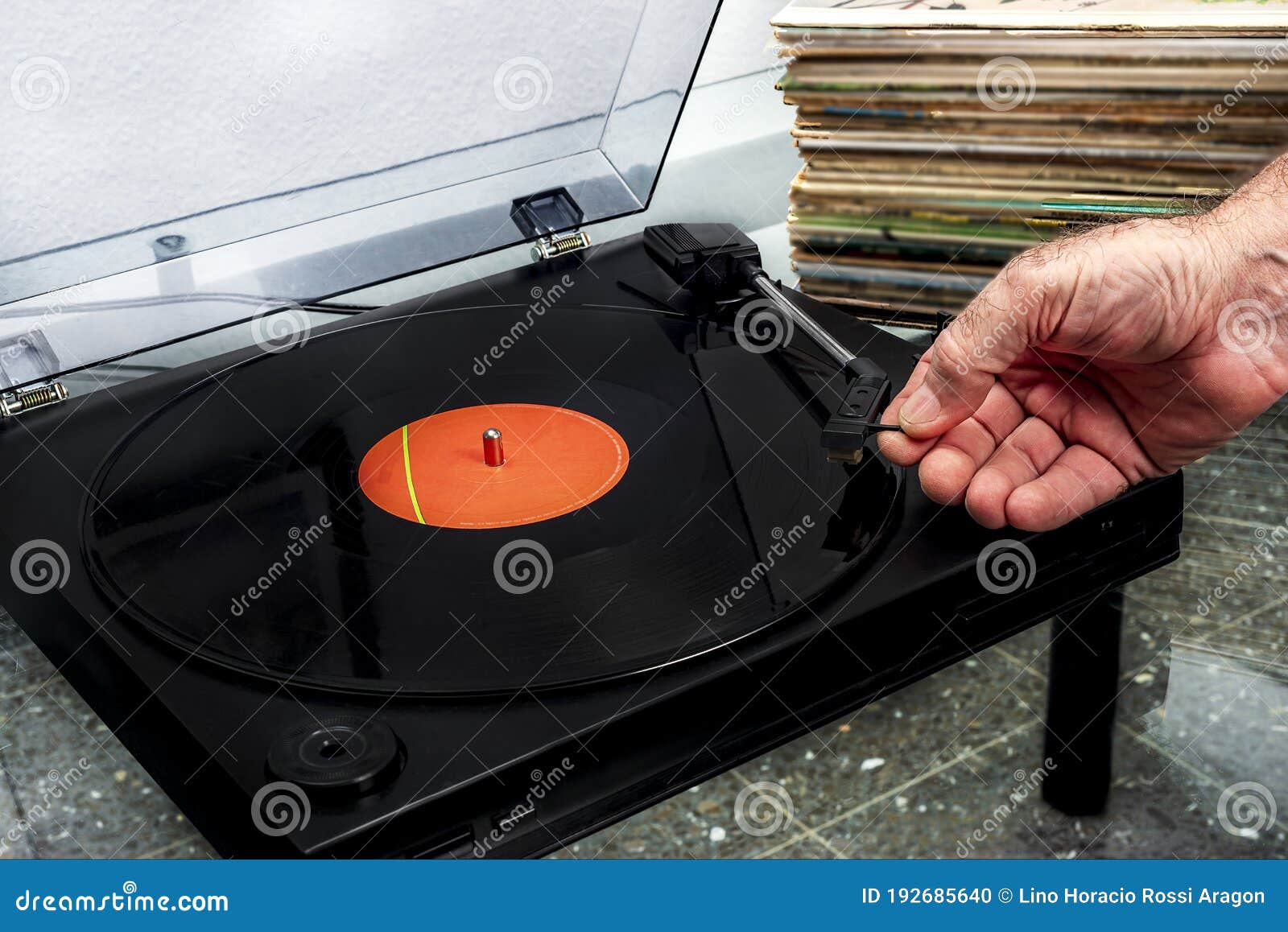 Hand Placing a Vinyl Record on a Record Player with a Stack of Vinyls ...