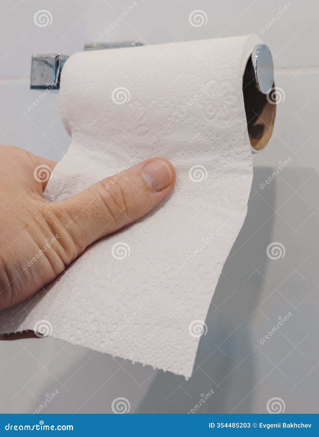 A Hand Pulls a Sheet of Toilet Paper from a Roll Mounted on the Wall in ...