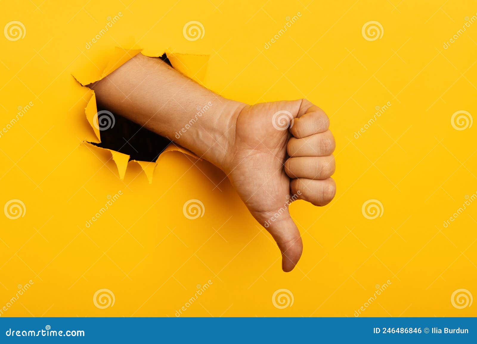 Hand Shows a Thumb Down through a Hole of Yellow Paper Wall Stock Photo ...