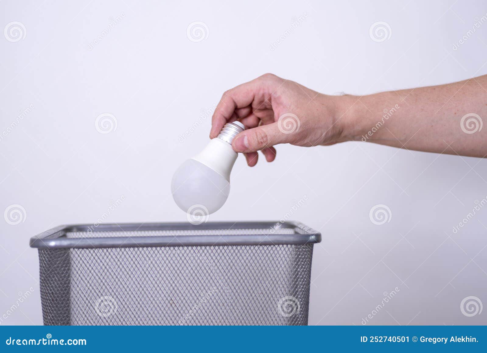 A Hand Throws a Light Bulb into a Trash Can Against a Gray Background ...