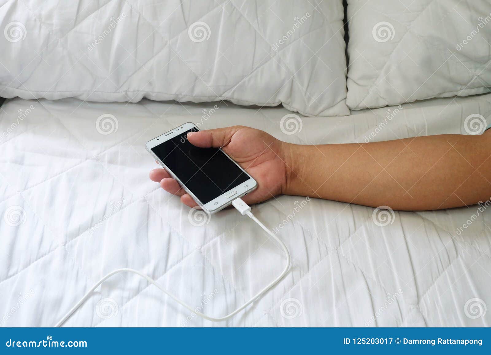Hand Using are Holding Mobile Phones. Charger is Plugged on the Bed ...