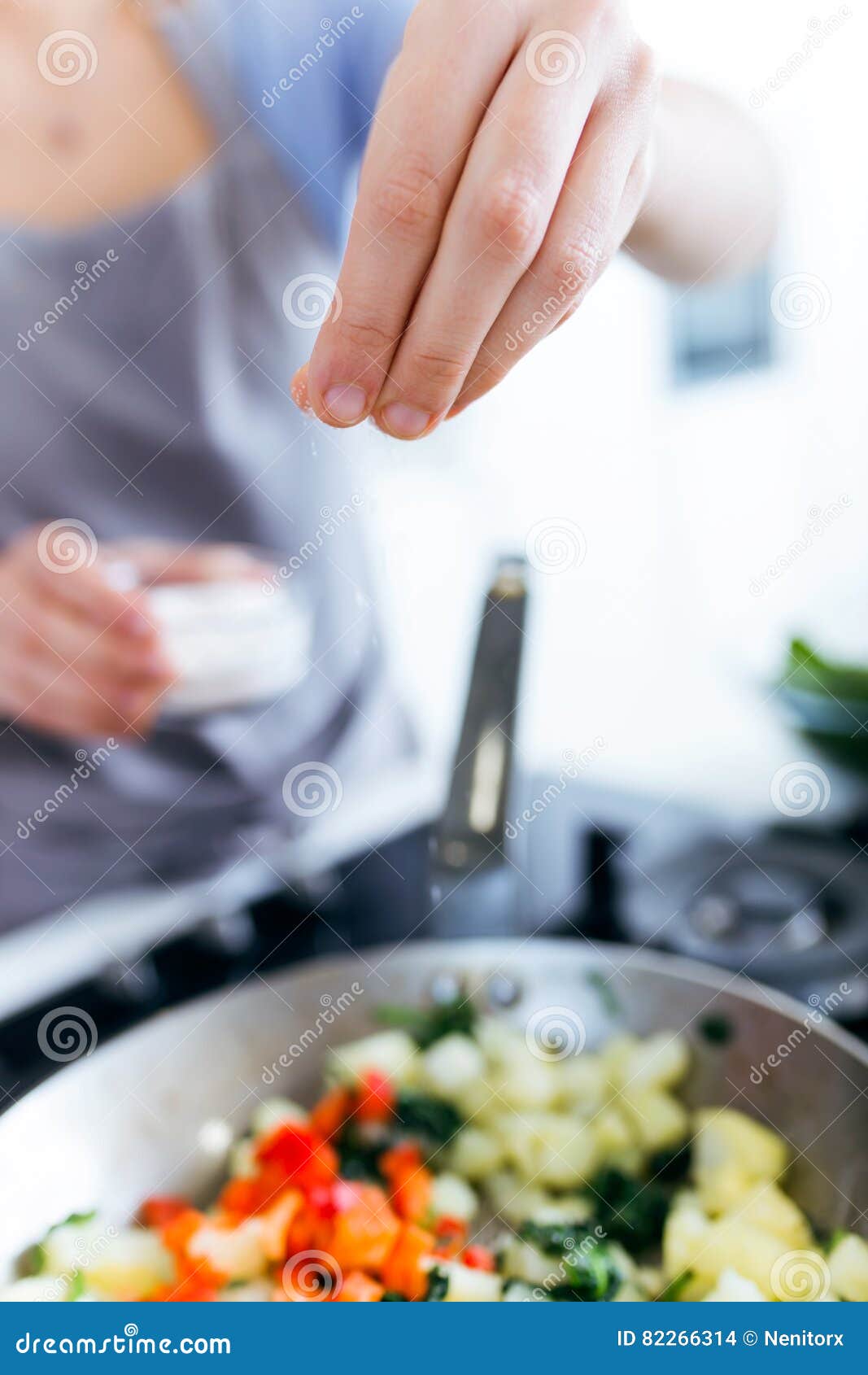 Hand of a Young Woman Adding Salt To Vegetables into the Pan. Stock ...