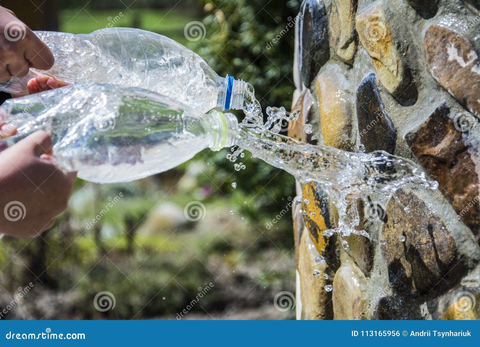 Hands Hold a Bottle of Water and Under Pressure, Sprinkle with a Jet of ...