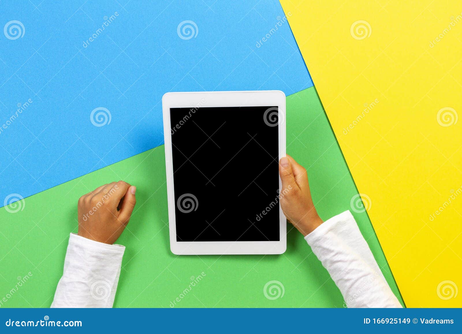 Hands Holding Tablet Computer on Yellow, Blue and Green Background. Top ...