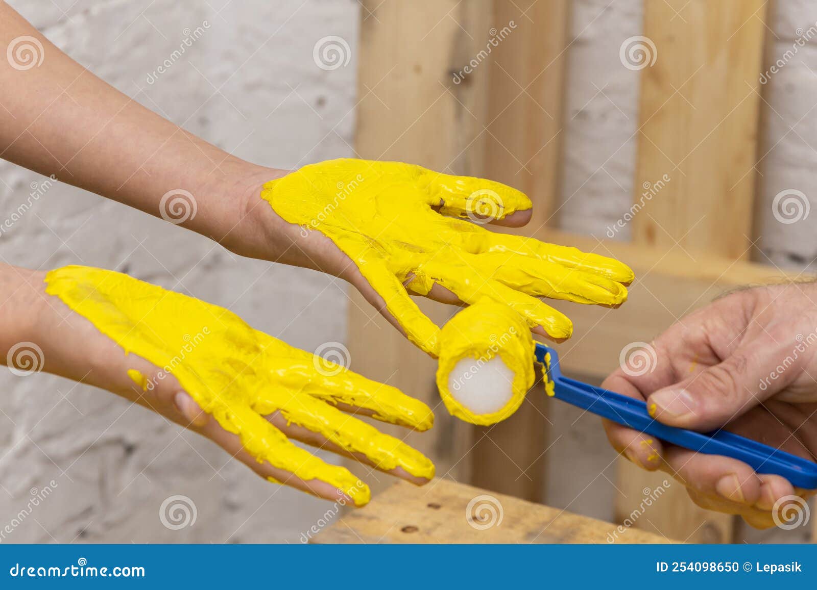The Hands are Painted with a Roller in Yellow Against a White Brick ...