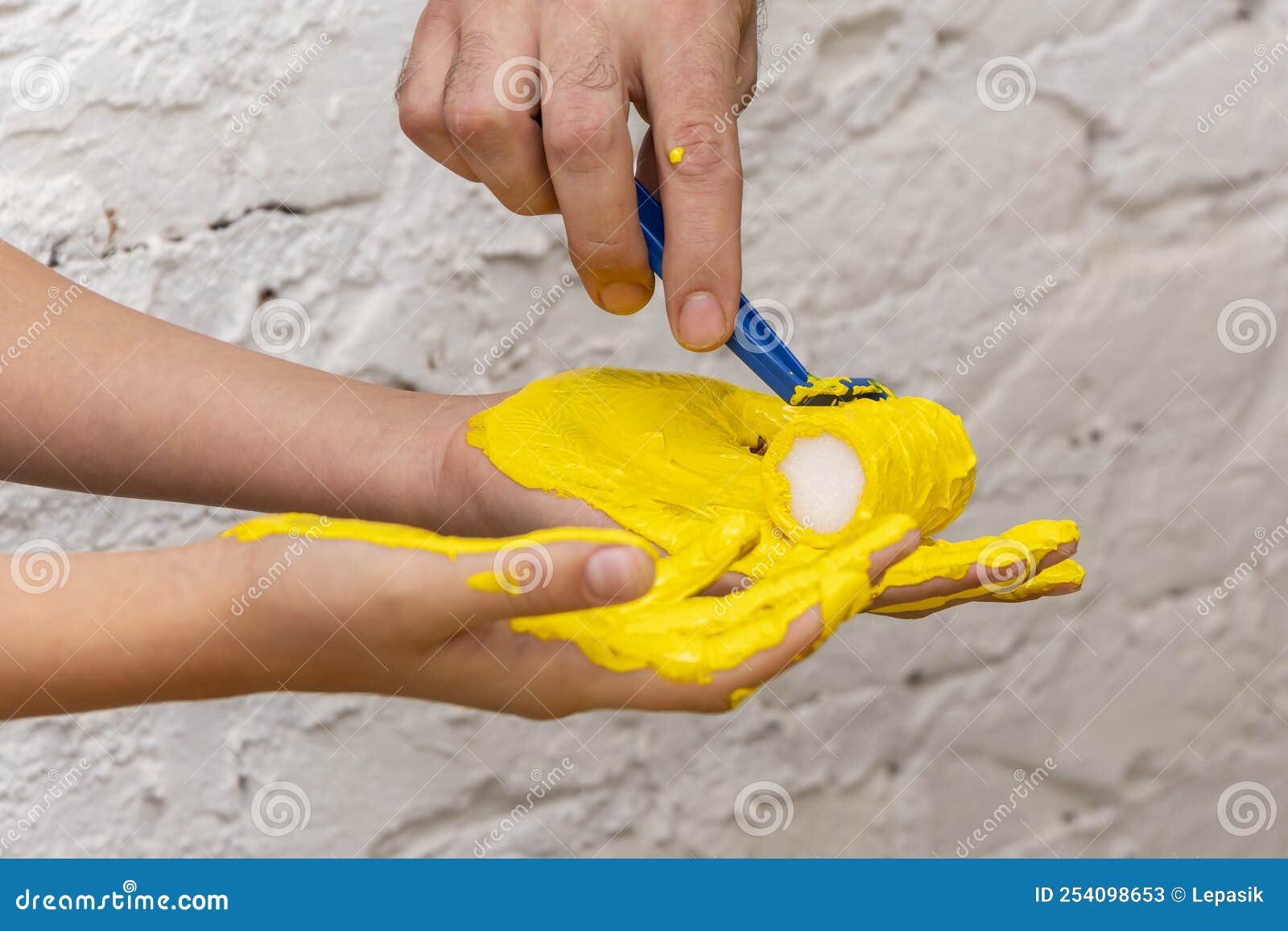 The Hands are Painted with a Roller in Yellow Against a White Brick ...