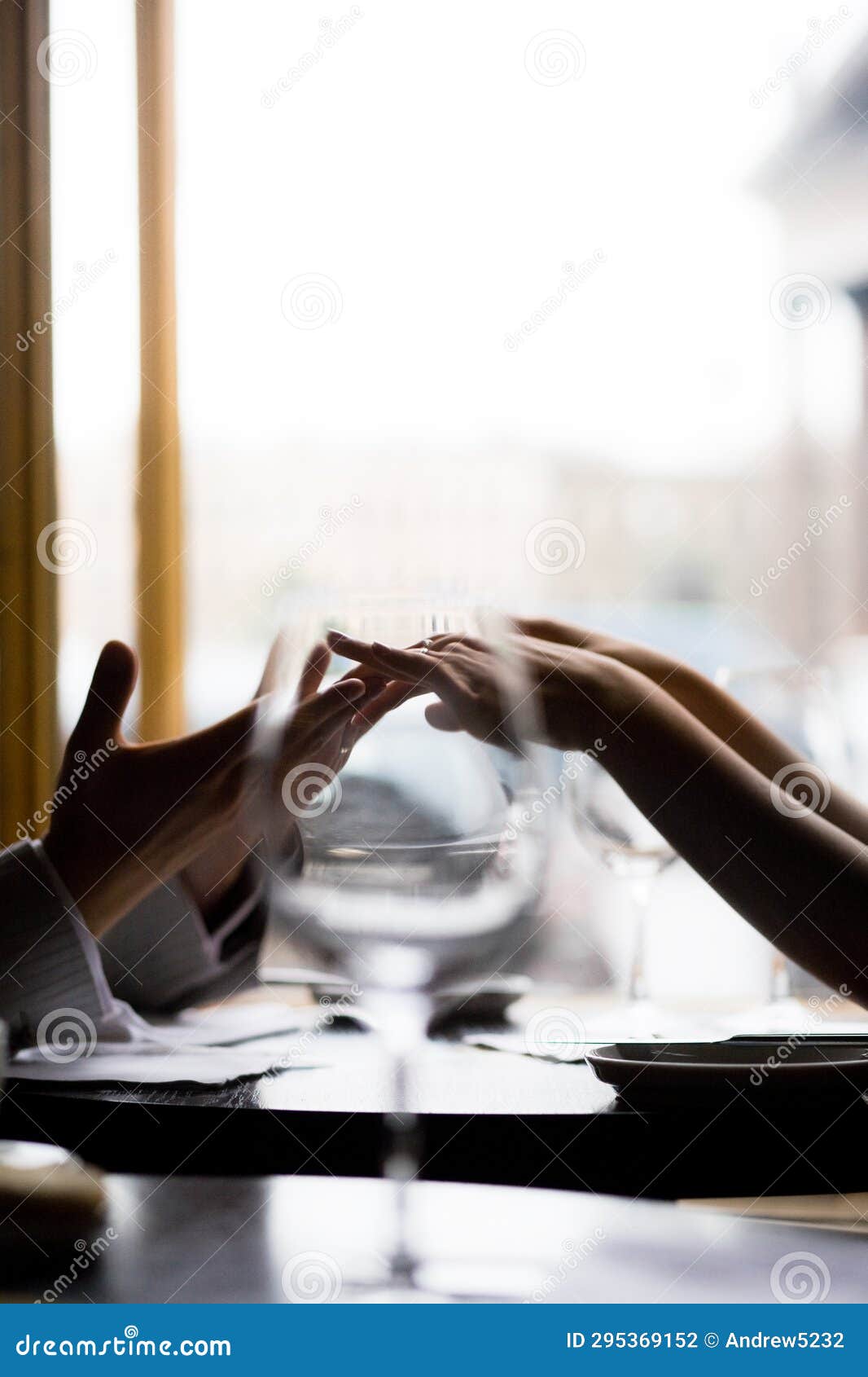 Hands Reaching Across a Table with Wine Glasses and a Window View in ...