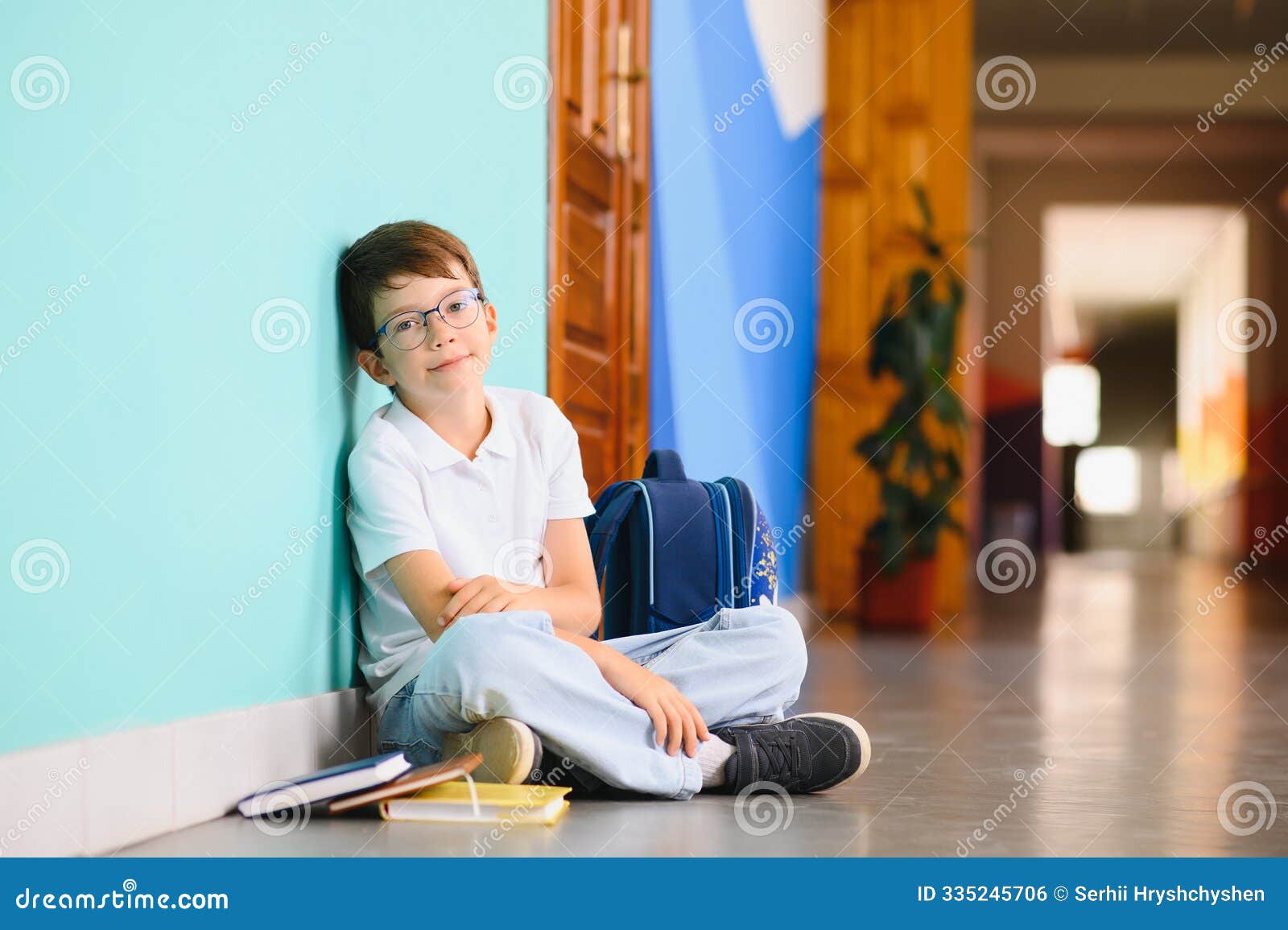 A Handsome Boy Student is Sitting on the Floor of the School Corridor ...