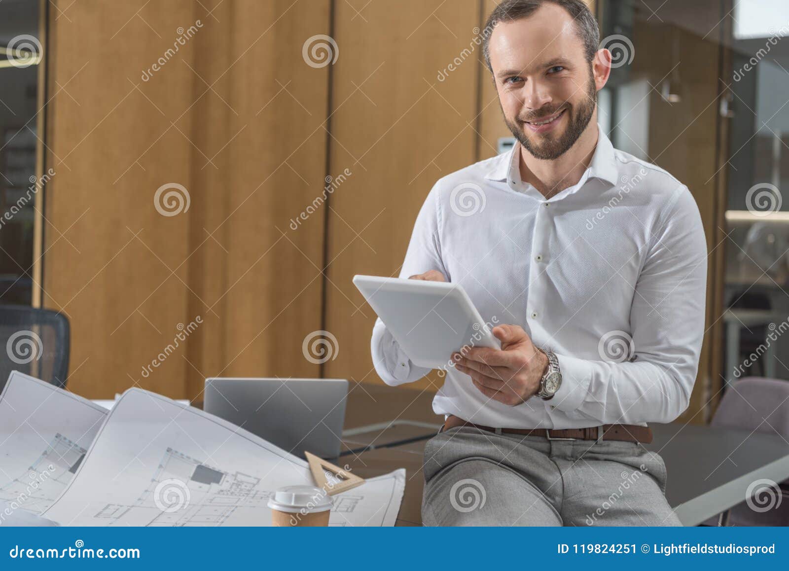 Handsome Happy Architect Sitting on Table with Plans and Using Tablet ...