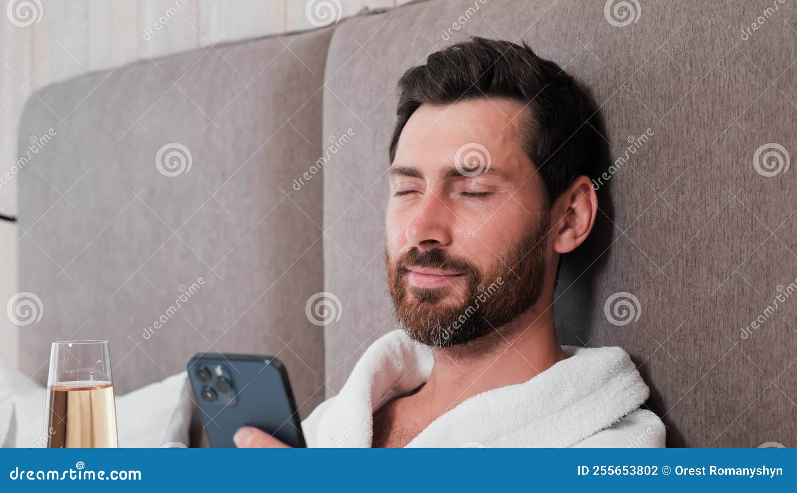 Handsome Man Sitting on the Bed in Bathrobe Reading Message in Mobile ... Handsome Man Sitting on the Bed in Bathrobe Reading Message in Mobile ...