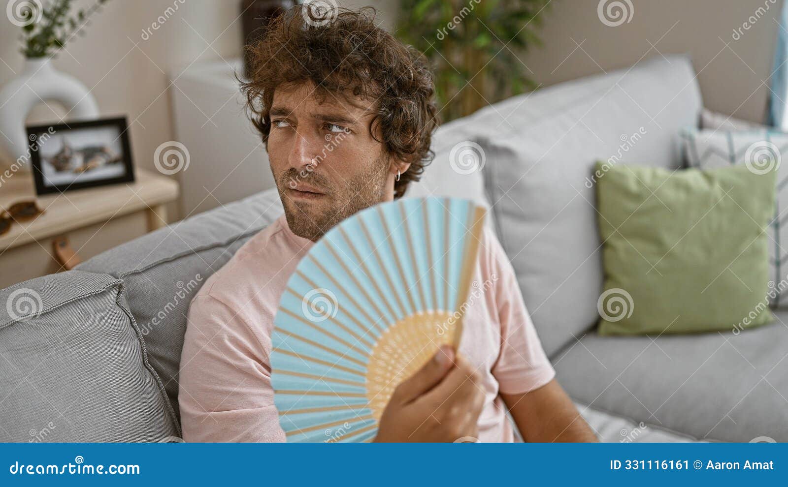Handsome Man Using Fan while Sitting on Couch Indoors, Looking Tired ...