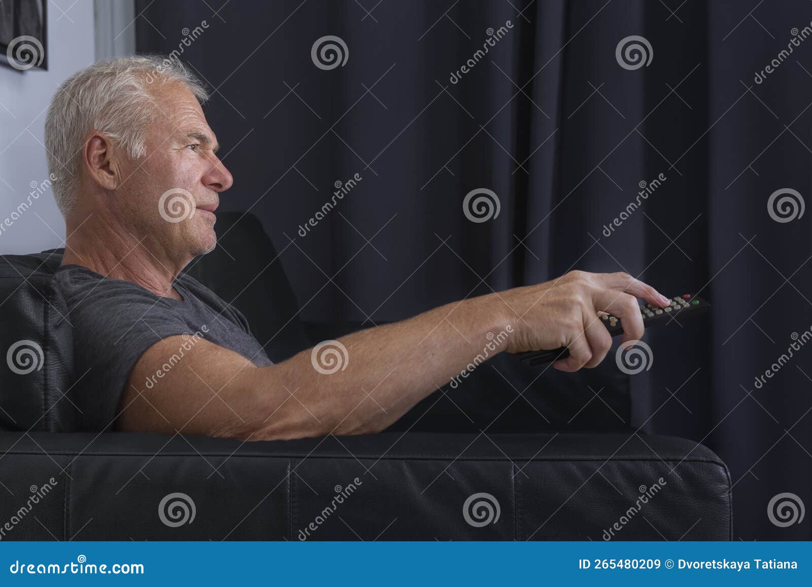 A Handsome Mature Man is Sitting on the Sofa with a Remote Control and ...